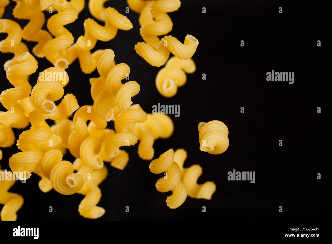 Falling cavatappi pasta. Flying yellow raw macaroni over black ...