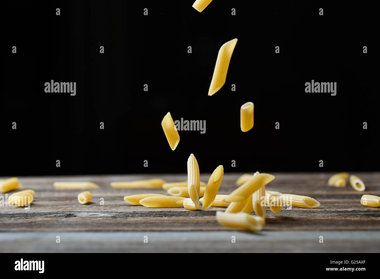 Falling penne pasta. Flying yellow raw macaroni over black background ...