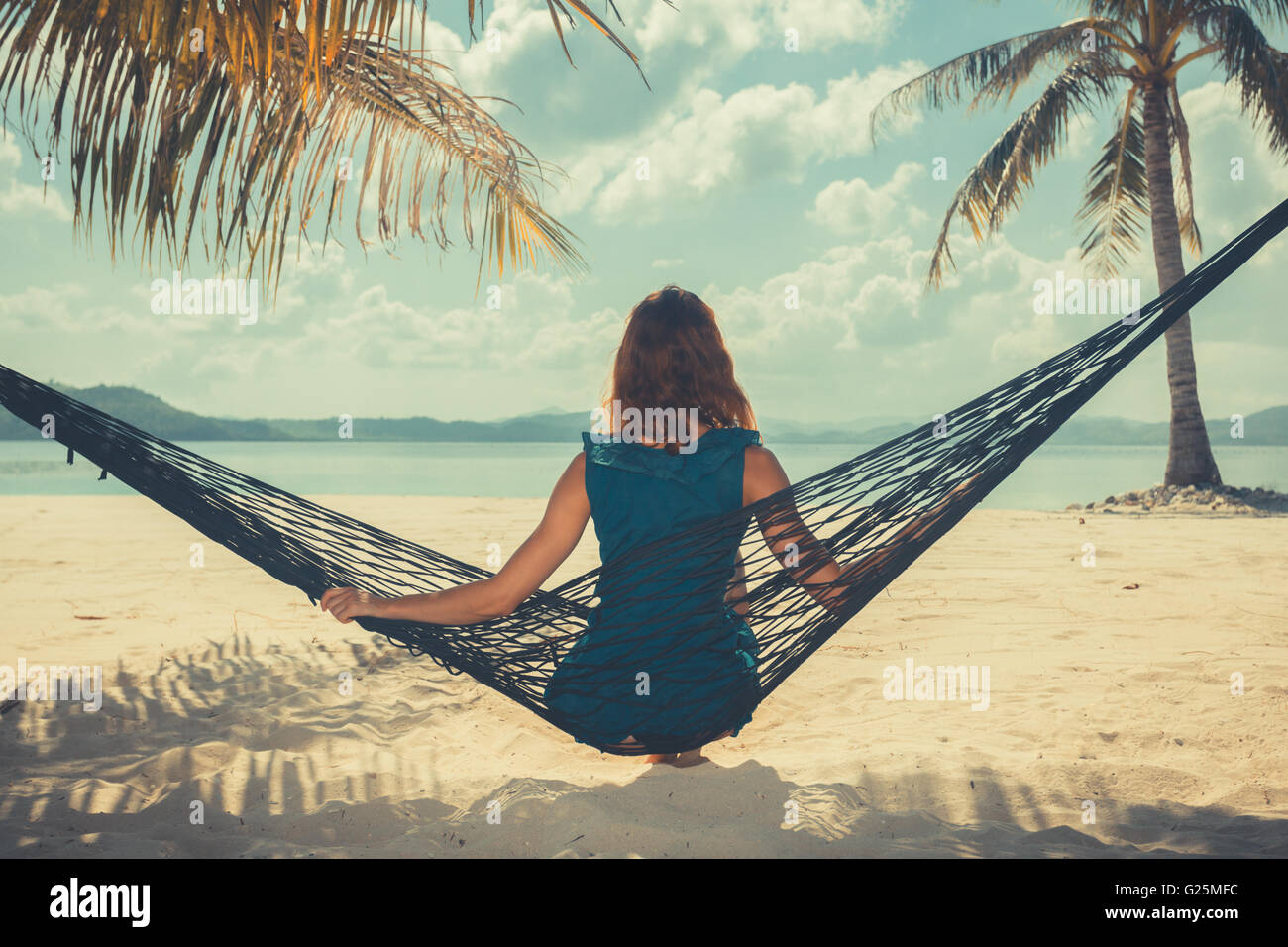 Vintage filtered shot of a young woman sitting in a hammock on a ...