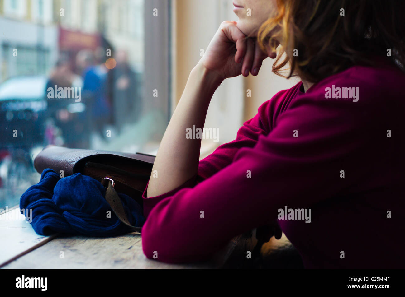 A young woman is sitting by a window and is looking out and day ...