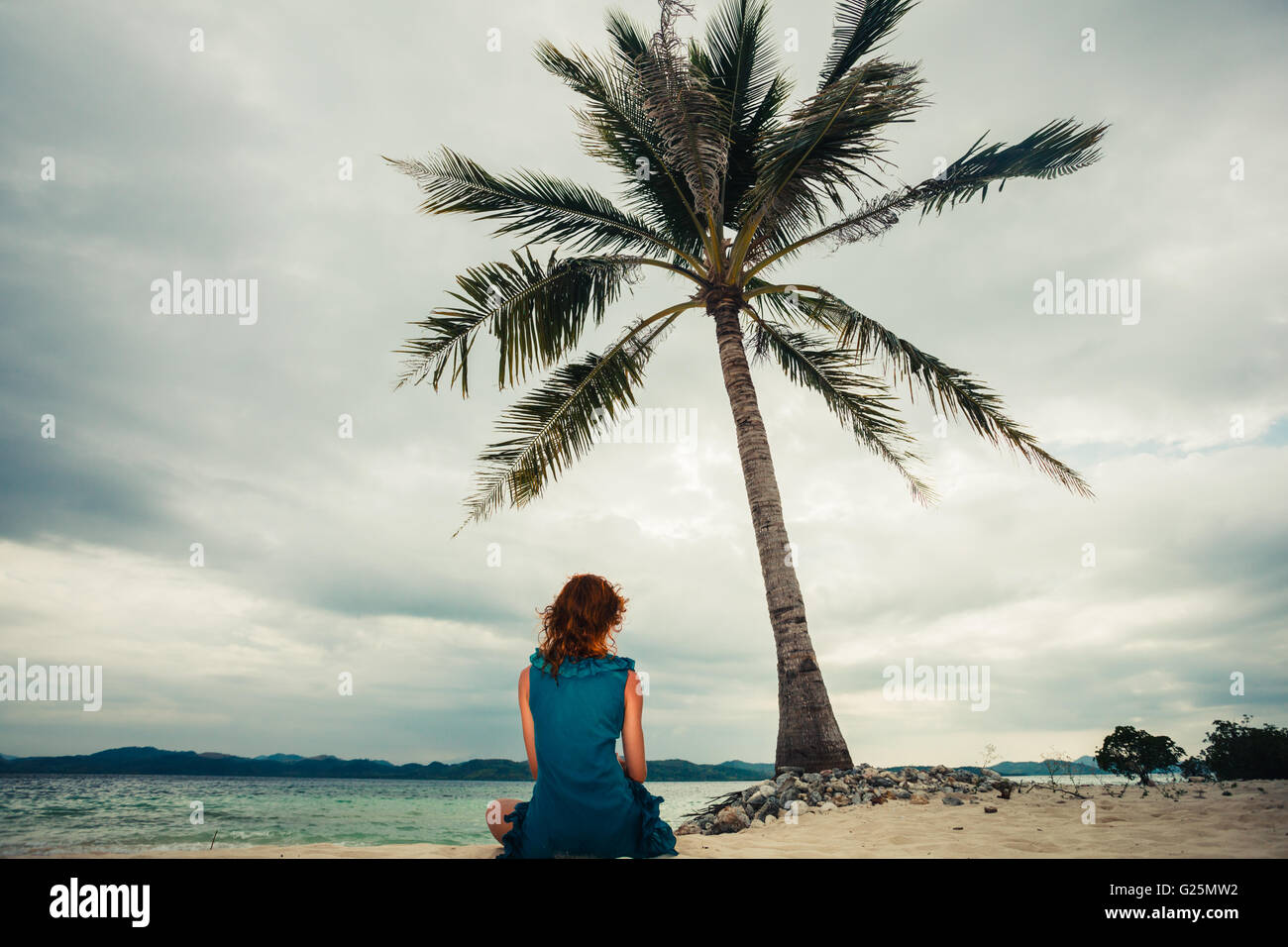 A young woman is sitting under a palm tree on a tropical beach Stock ...