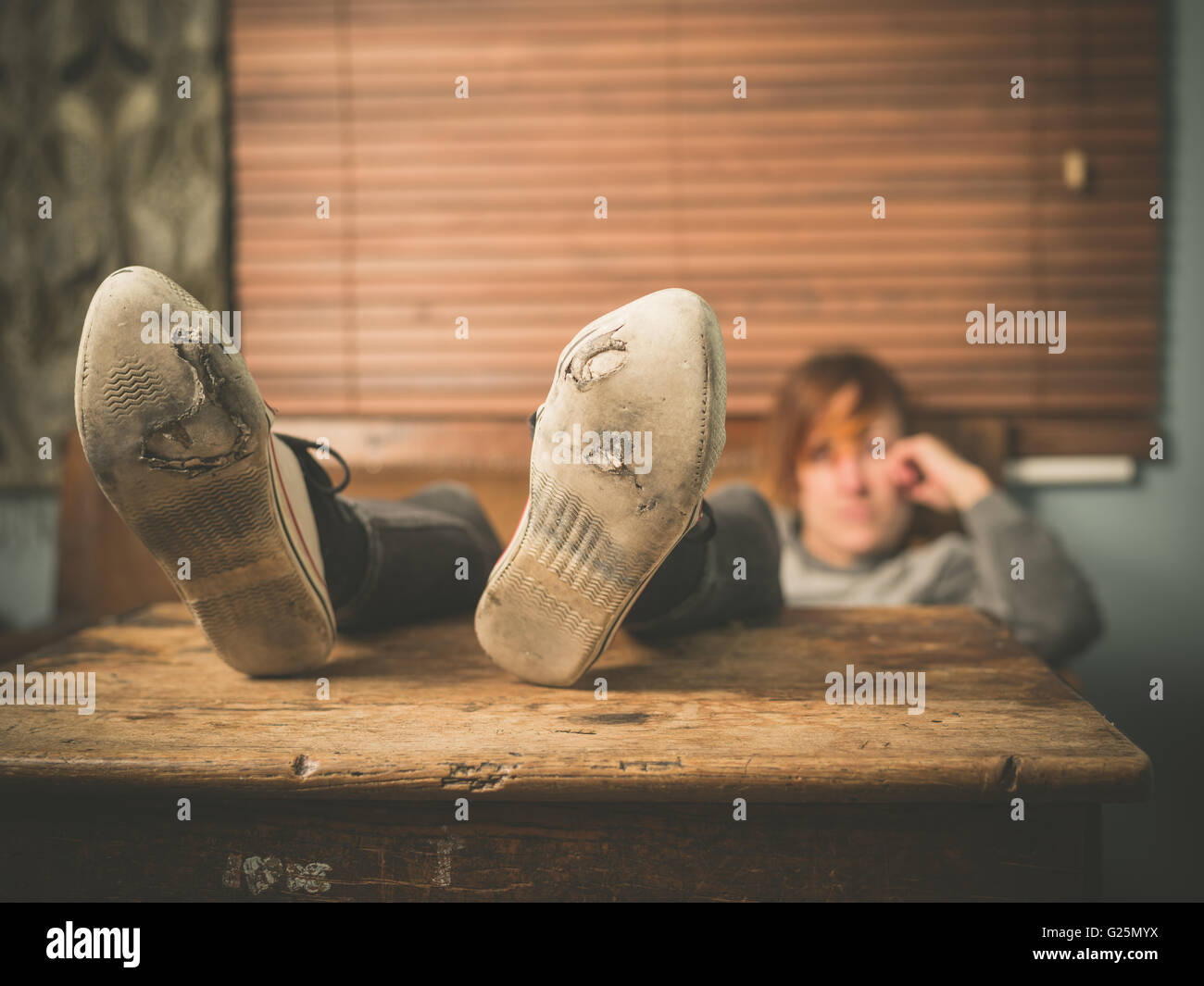 A young woman wearing worn out shoes is resting her feet on a table at ...