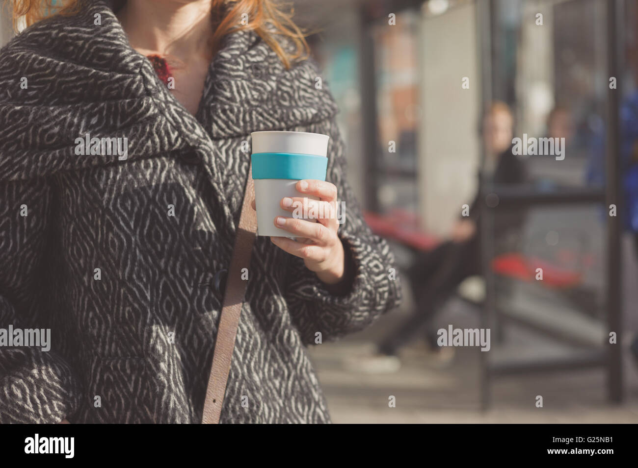 A young woman is waiting at a bus stop with a cup of coffee Stock Photo ...