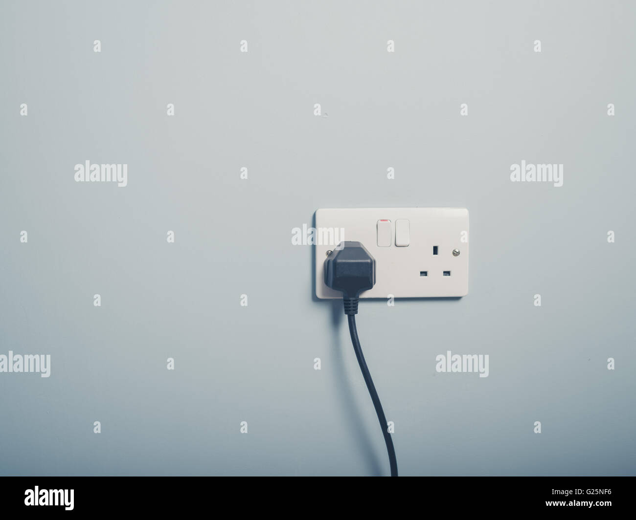 A United Kingdom standard wall socket on a blue wall with a cord ...