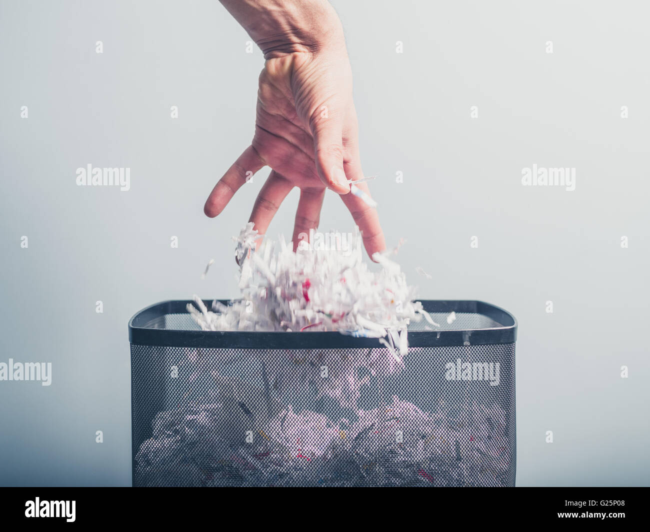 A hand is putting a bunch of shredded paper in a waste paper basket ...