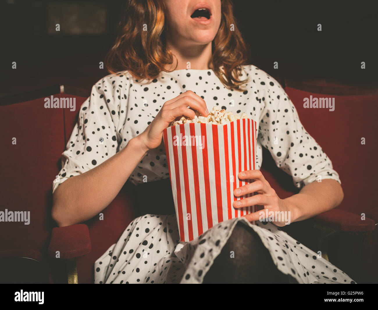 A young woman is sitting on the front row in a movie theater and is ...