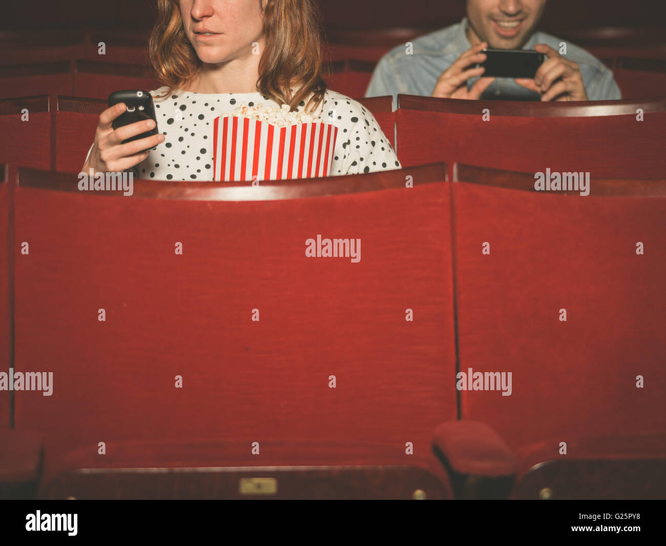 A young man and woman are using their phones in a movie theater Stock ...