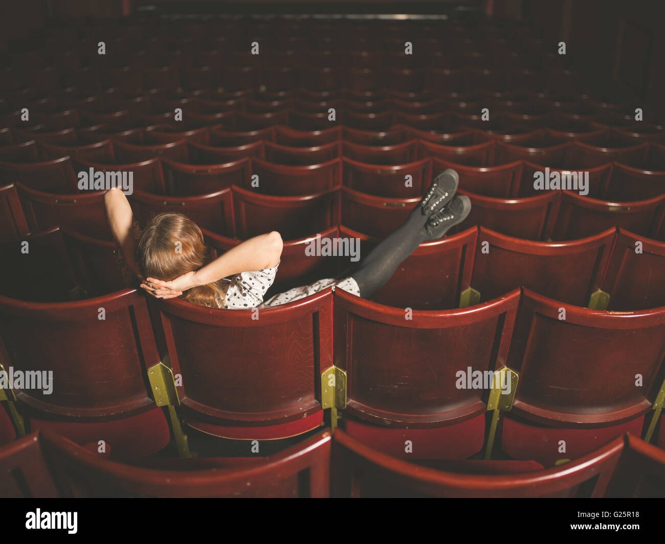 A young woman is sitting in an auditorium with her feet on the seats in ...