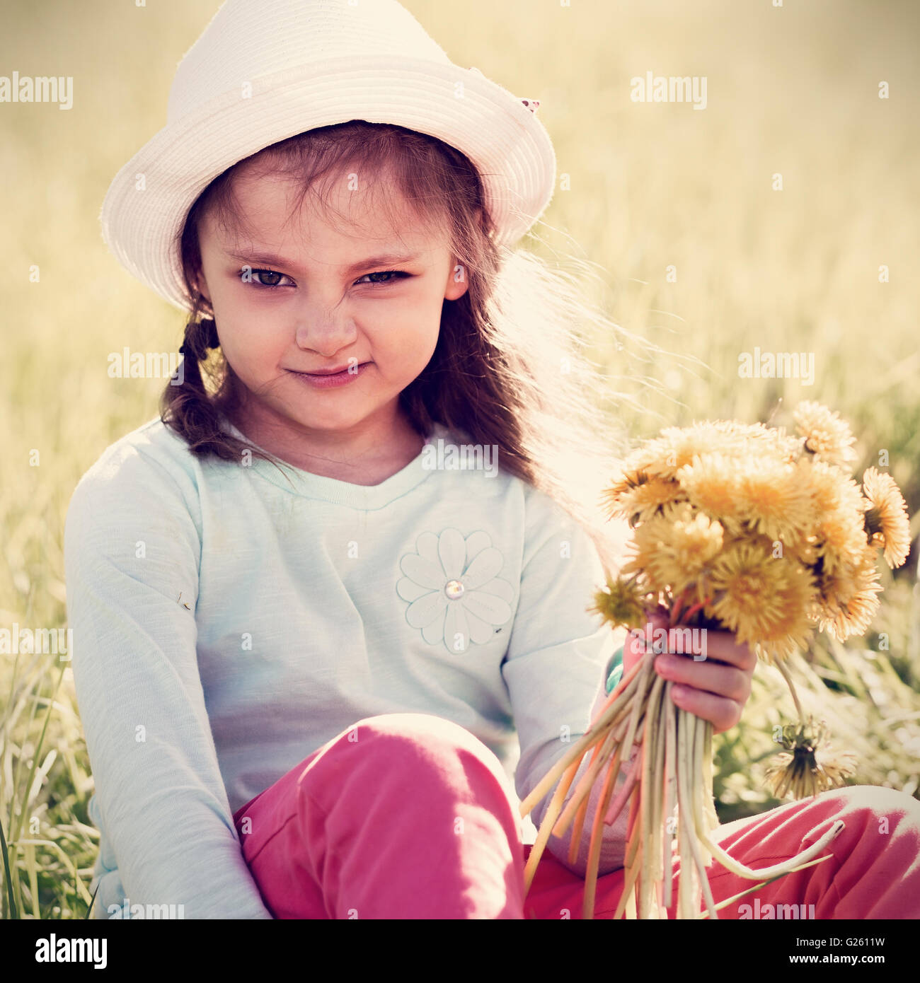 Funny grimacing kid girl in fashion hat sitting on the grass and ...