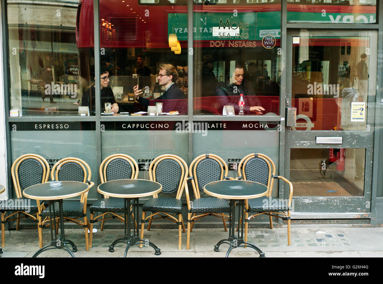 Cafe with empty tables and chairs outside with people inside looking ...