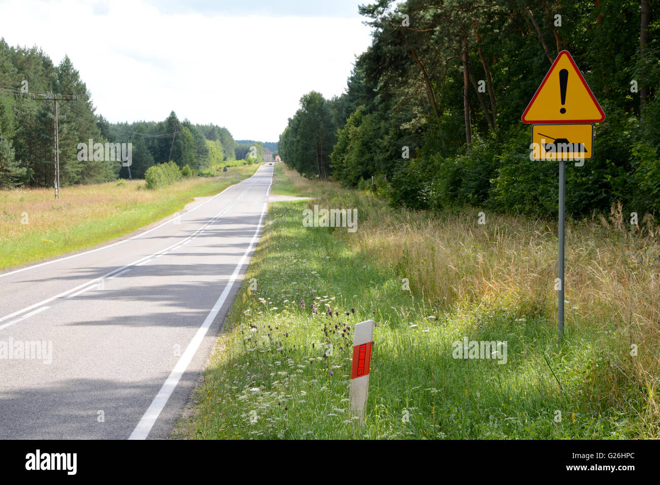 Yellow tank warning road sign standing at tarmac road at military ...