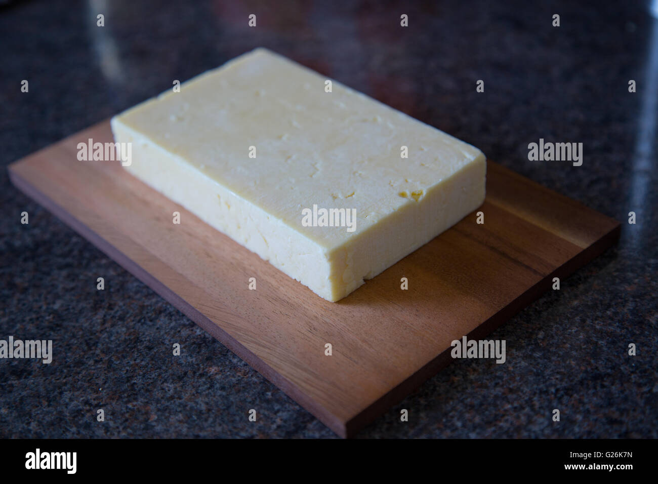 a block of cheddar sitting on a wooden cheeseboard Stock Photo - Alamy