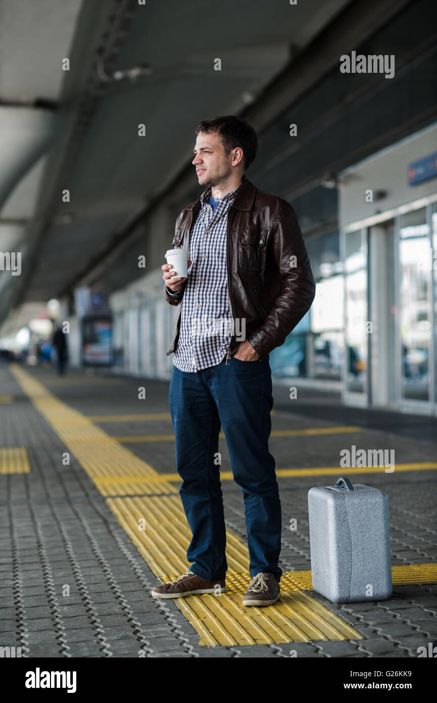 Young regular man standing waiting near the airport with cup of coffee ...