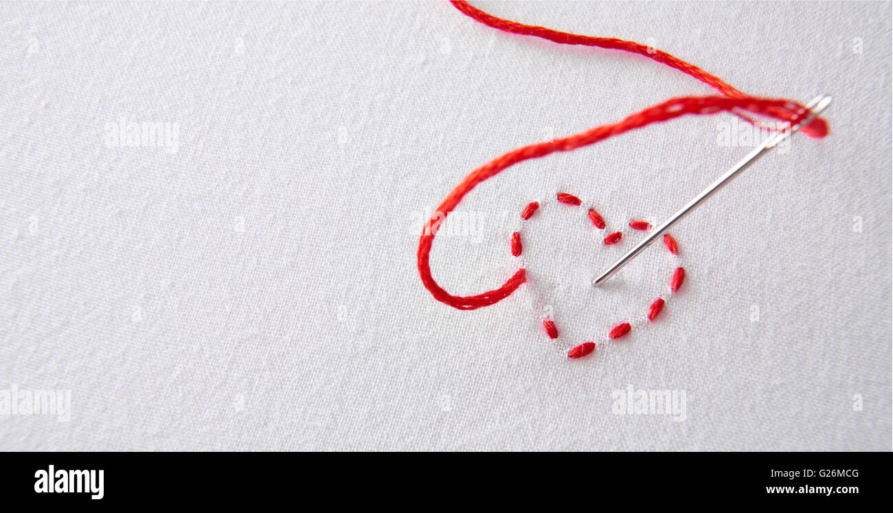 Embroidered red heart on a white cloth with needle punctured. Concept ...