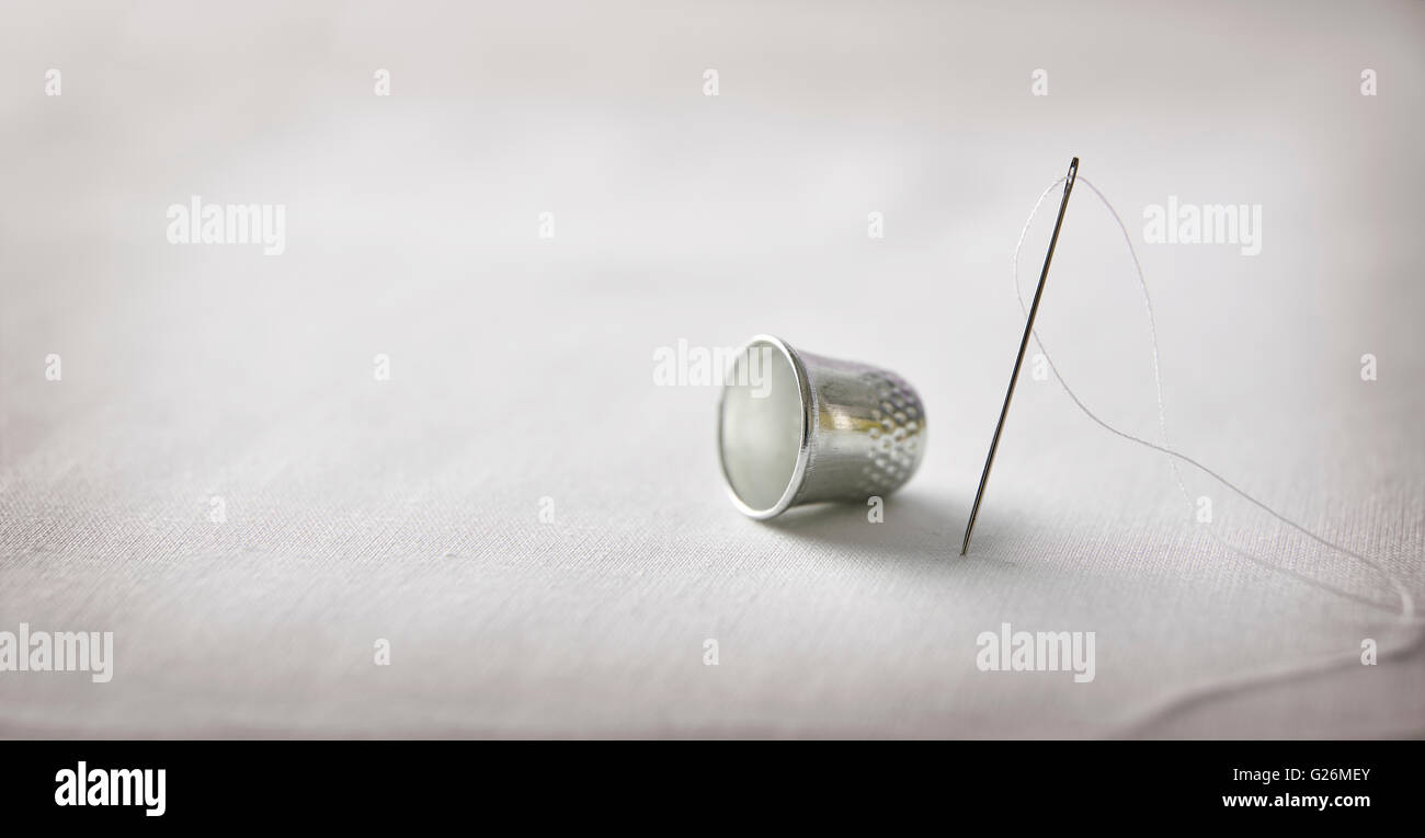 Needle with thread and thimble on white fabric background. Horizontal ...