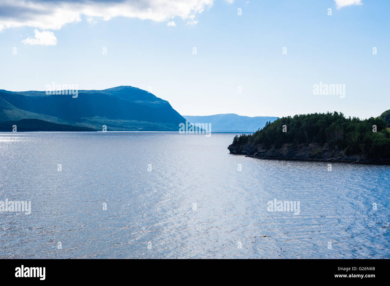 Ocean inlet among forested green mountains and shore under blue sky ...