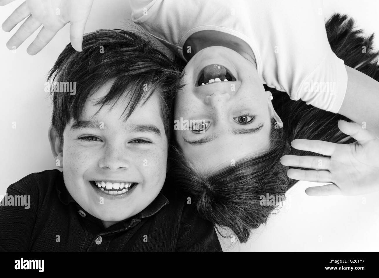 Cheeky children pulling funny faces at each other whilst laying on the ...