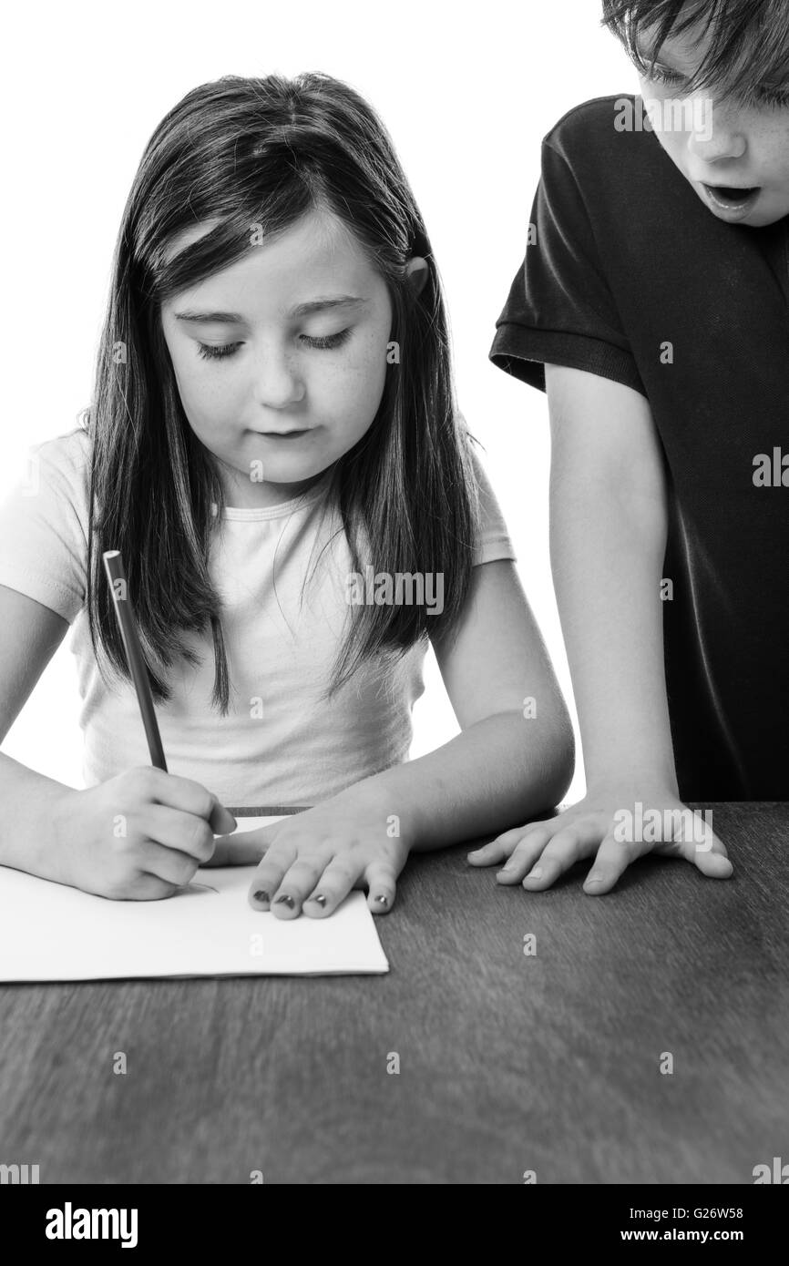 Young girl is doing her homework whilst her brother looks on in ...