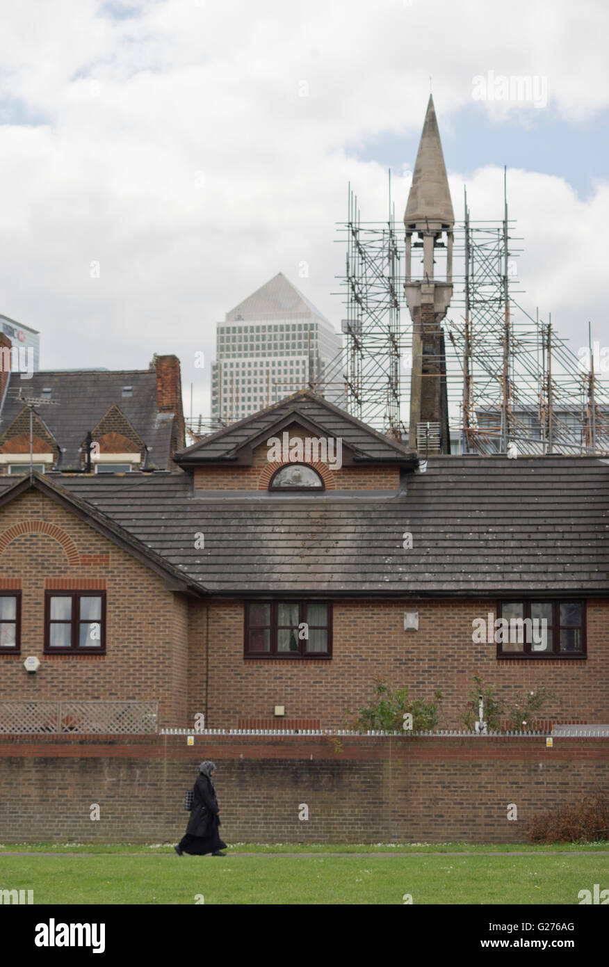Muslim woman walks past mosque being refurbished, with Canary Wharf in ...