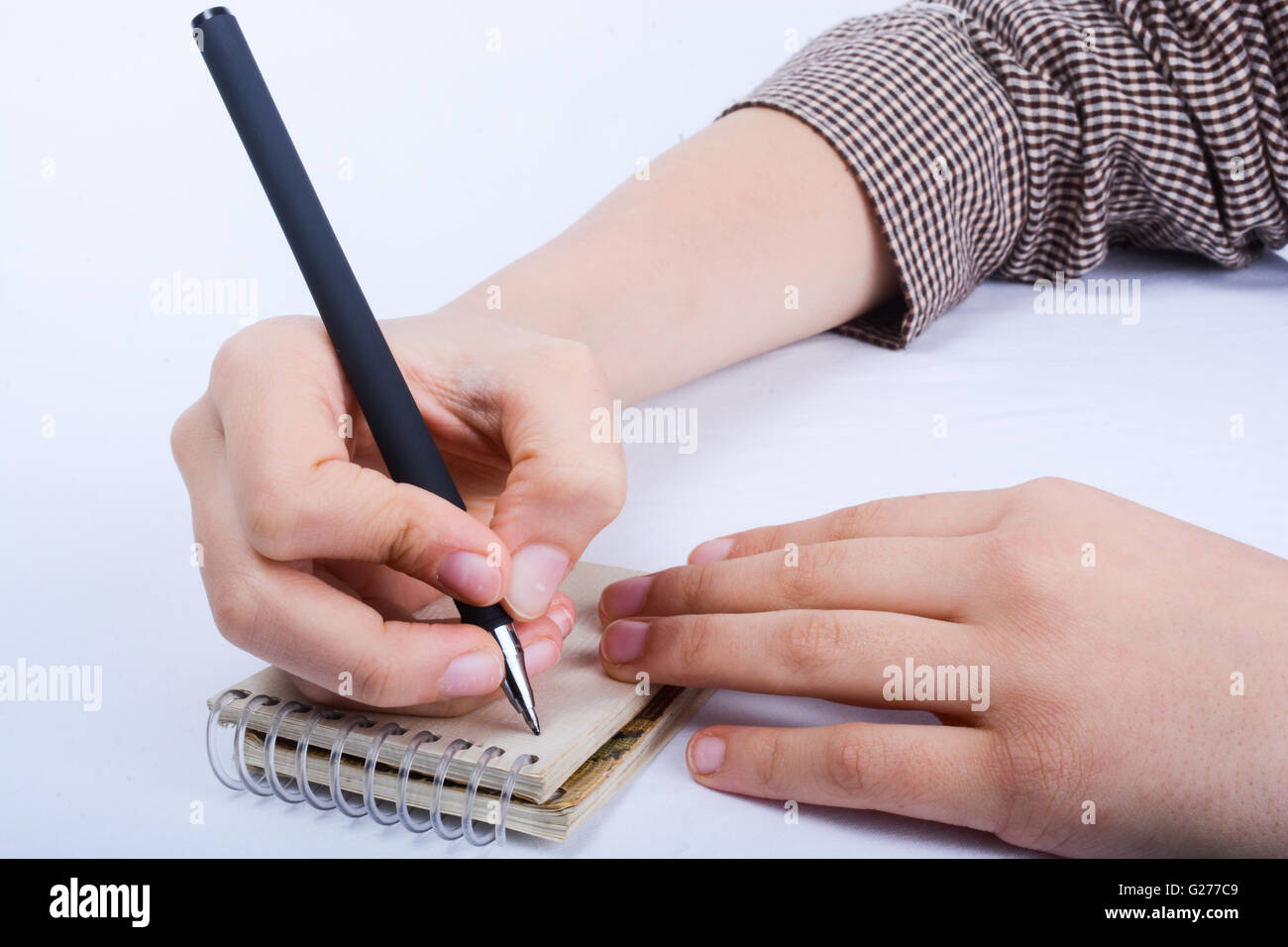 A child hand is writing with pen on a spiral notebook on white ...