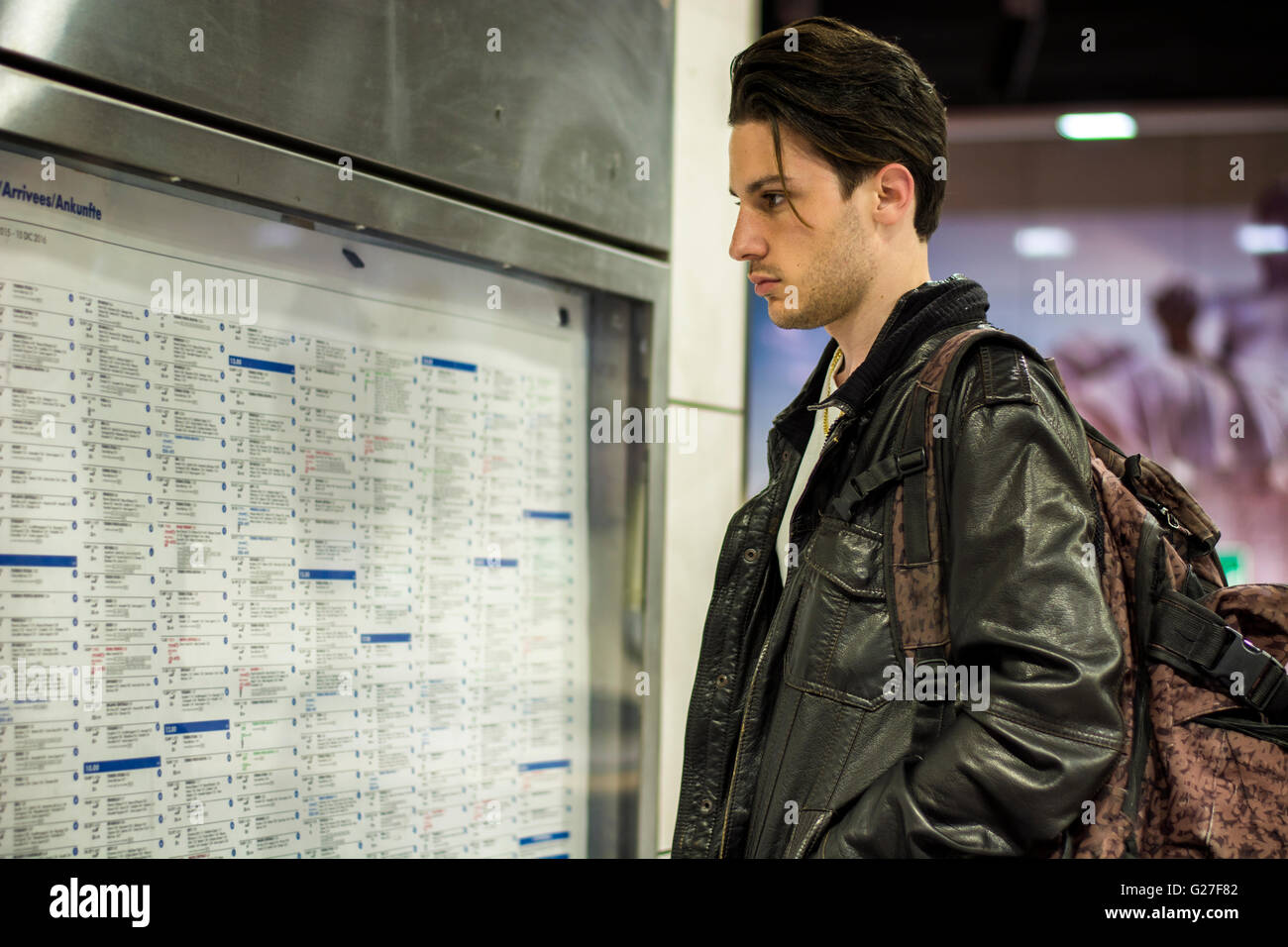 Young man traveling, standing next to train timetable in railway ...