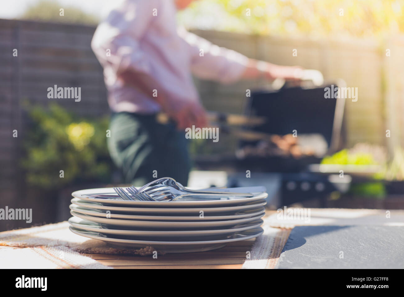 Stack of plates on a table outside in a garden with a man attending to ...