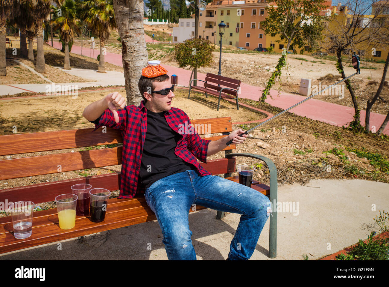 Guy documenting his hangover on a park bench with a selfie, a concept ...