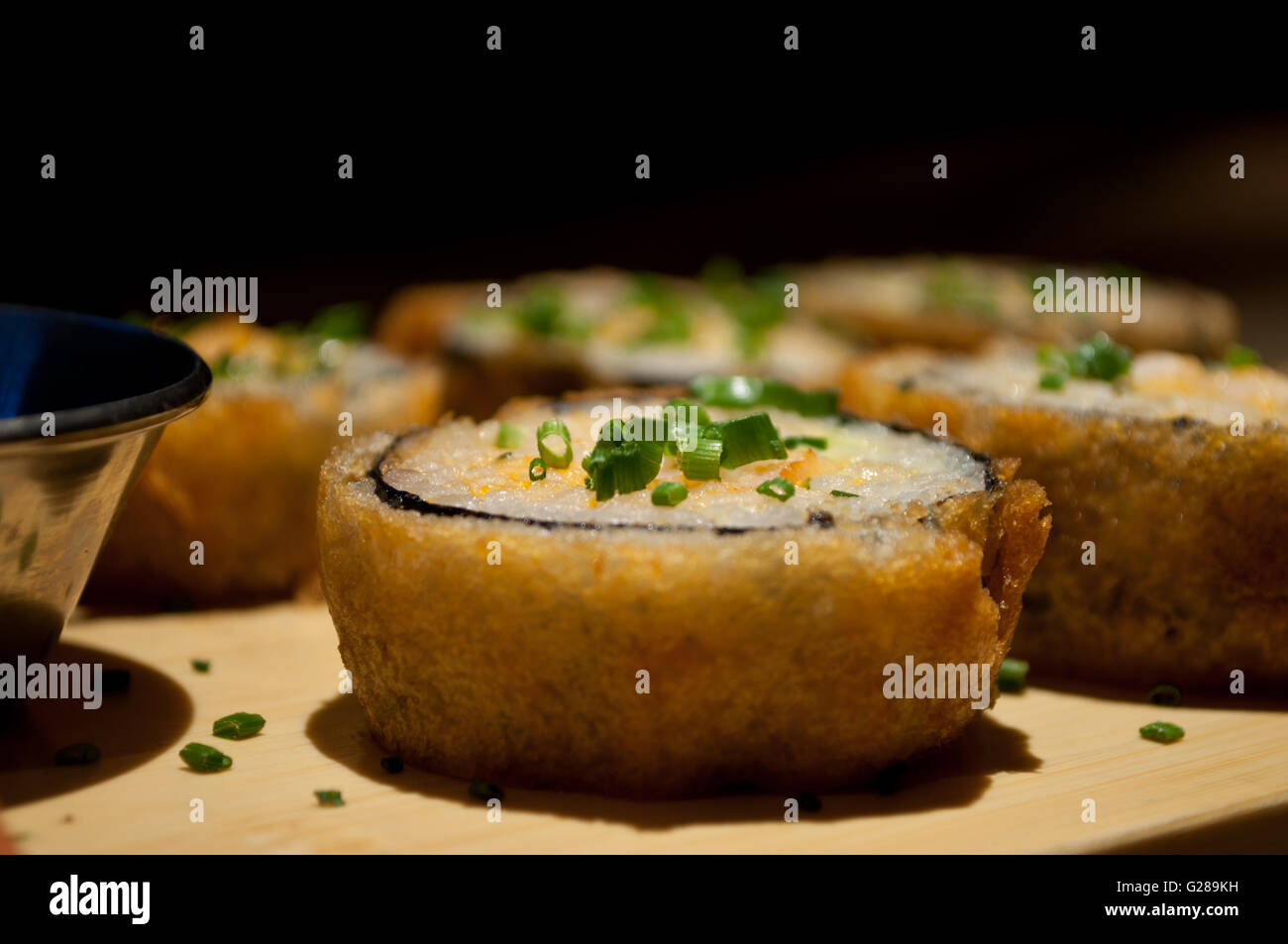 Deep fried sushi topped with chives served on a wooden platter (close ...