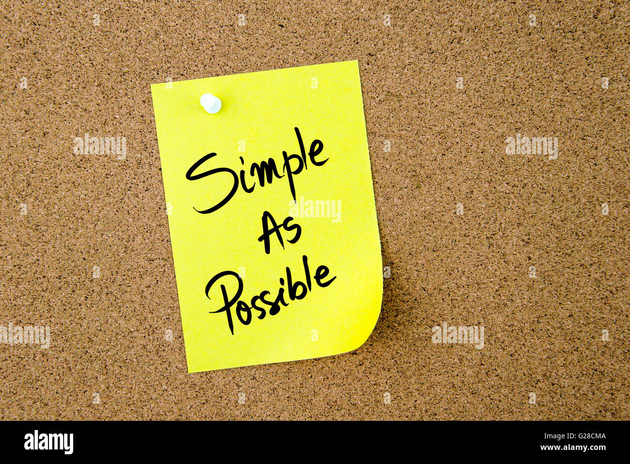 Simple As Possible written on yellow paper note pinned on cork board ...