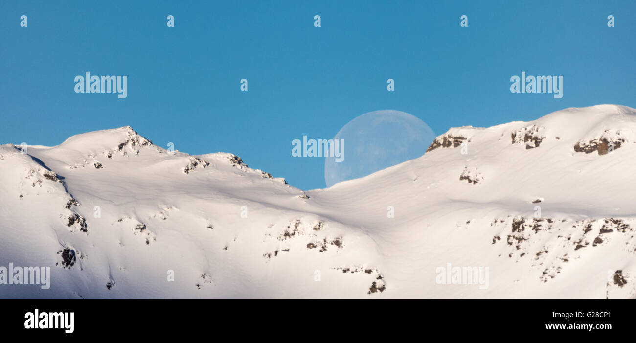 Moon falling setting part eclipsed behind snow covered French Alpes ...