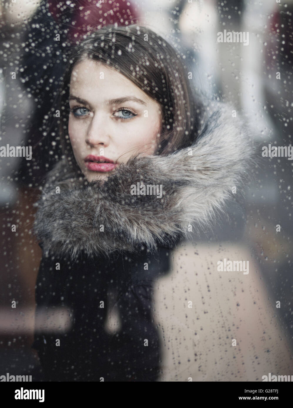 Portrait of a young woman on a rainy day looking through the window ...
