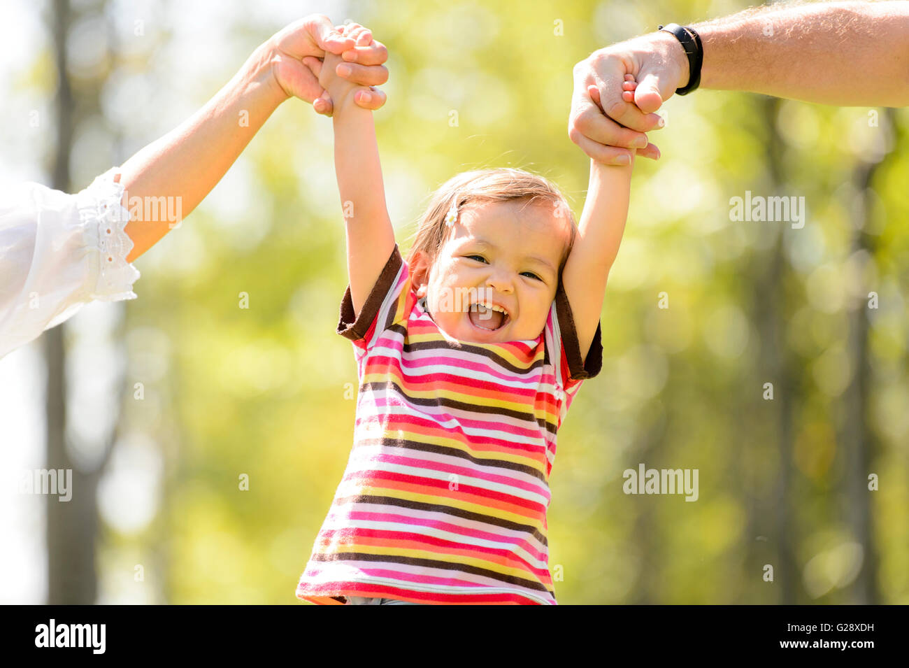 Toddler holding parents hands in a park Stock Photo - Alamy