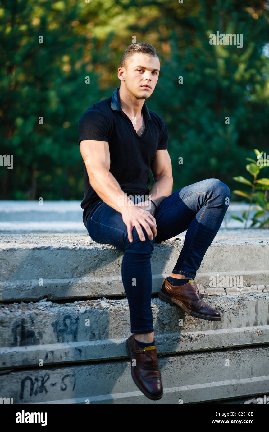Muscular young man sitting on concrete slab Stock Photo - Alamy