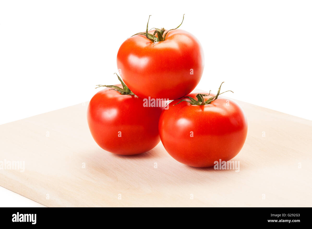 Three perfect red tomatoes arranged on wooden board with white ...