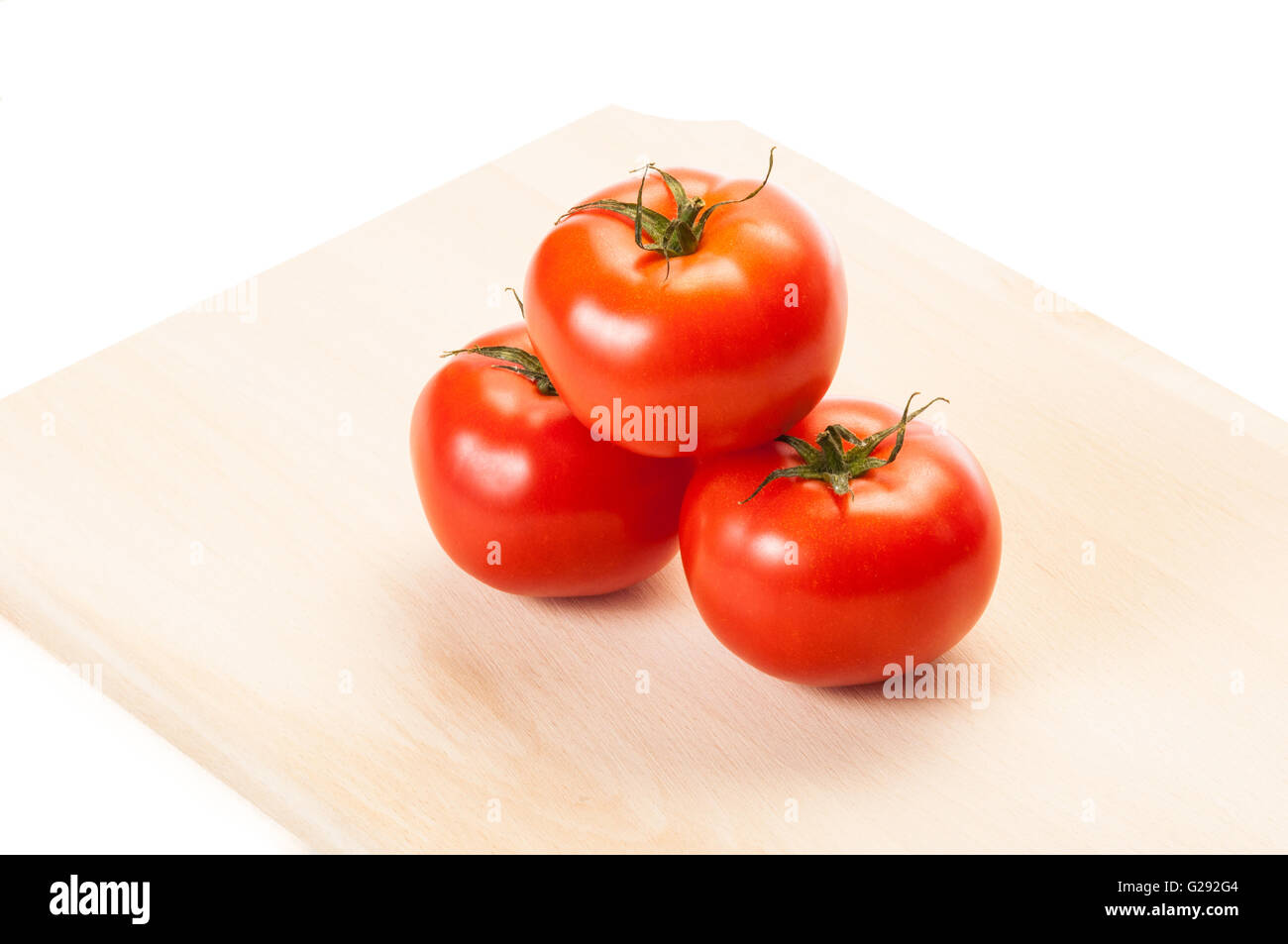 Three perfect red tomatoes arranged on wooden board with white ...