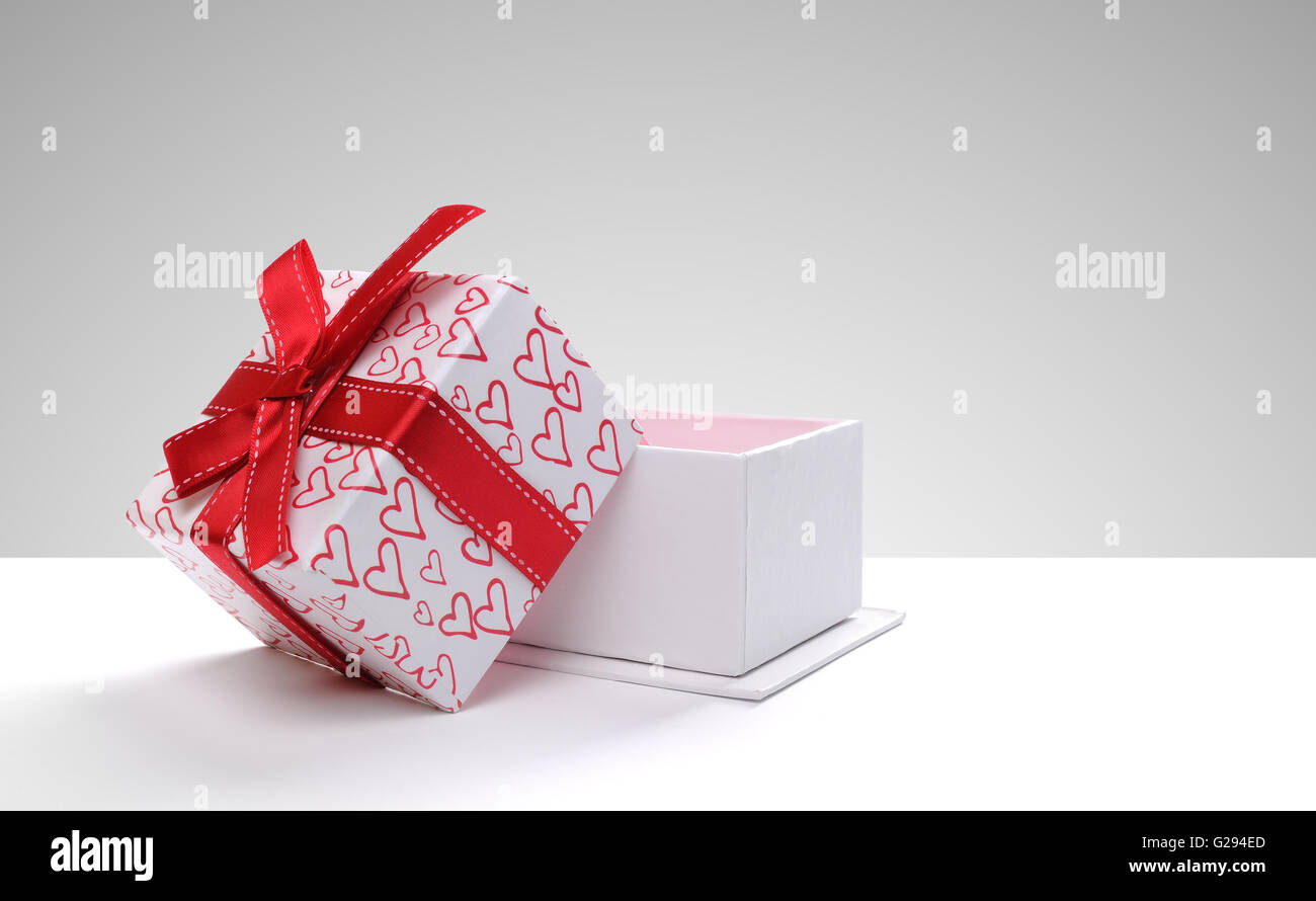 Decorative open gift box with red ribbon and hearts printed on white ...