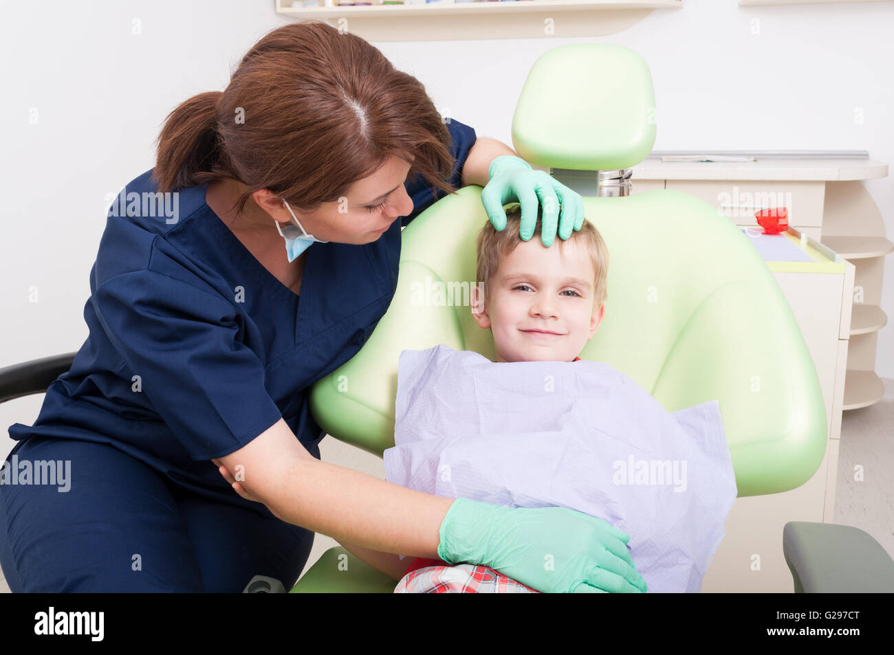 Protective dentist woman with son patient sitting in dentist chair ...