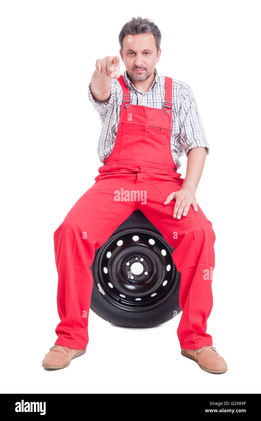 Mechanic pointing finger to the camera witting on tire isolated on ...