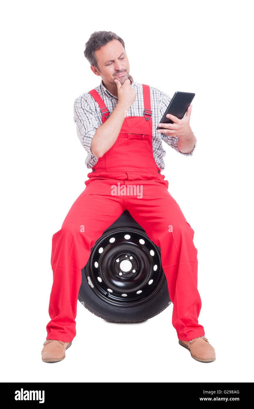 Smart mechanic reading from wireless tablet and sitting on car wheel ...