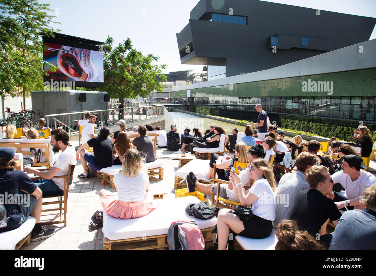 Attendees sit outside in the sunshin watching the talks from the main ...