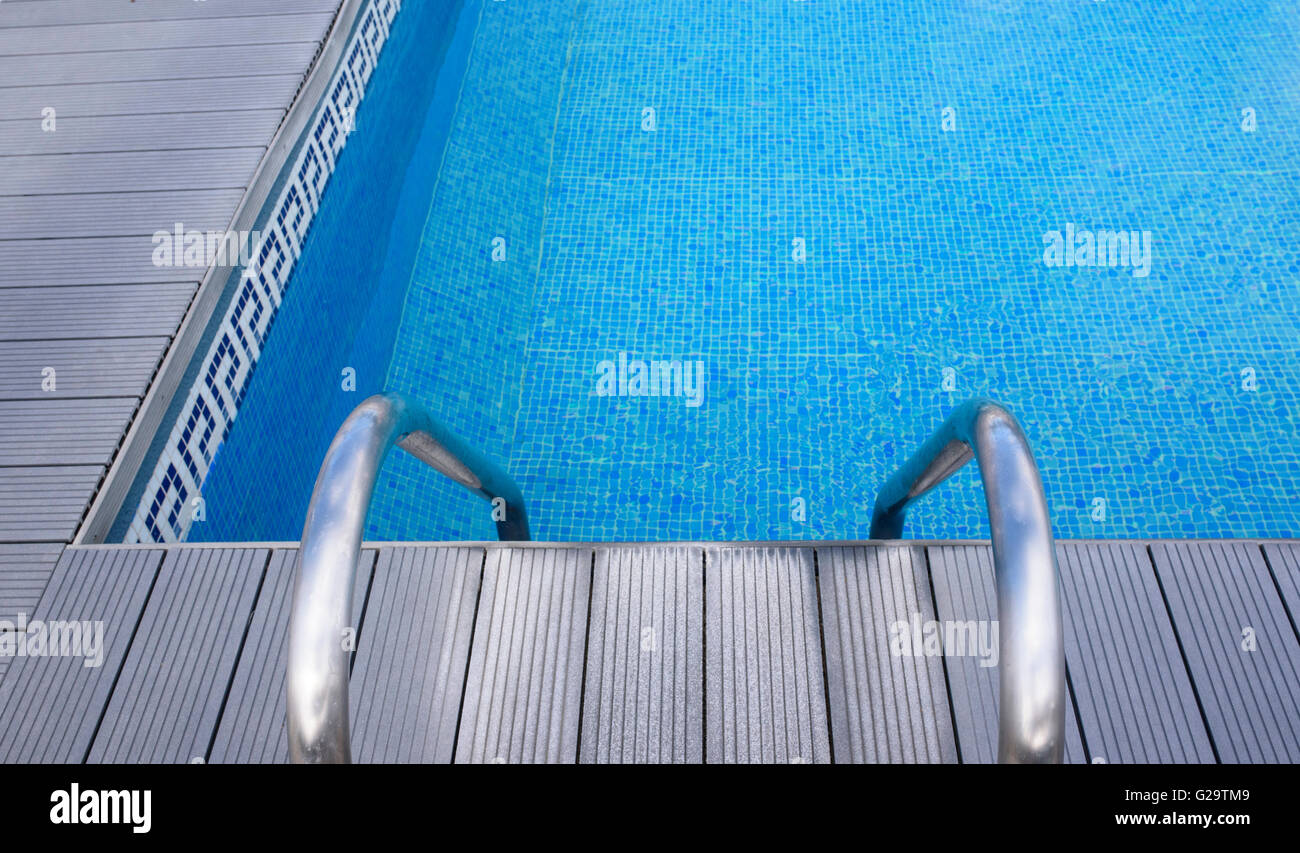 Metal steps leading into an outdoor swimming pool edged with decking ...