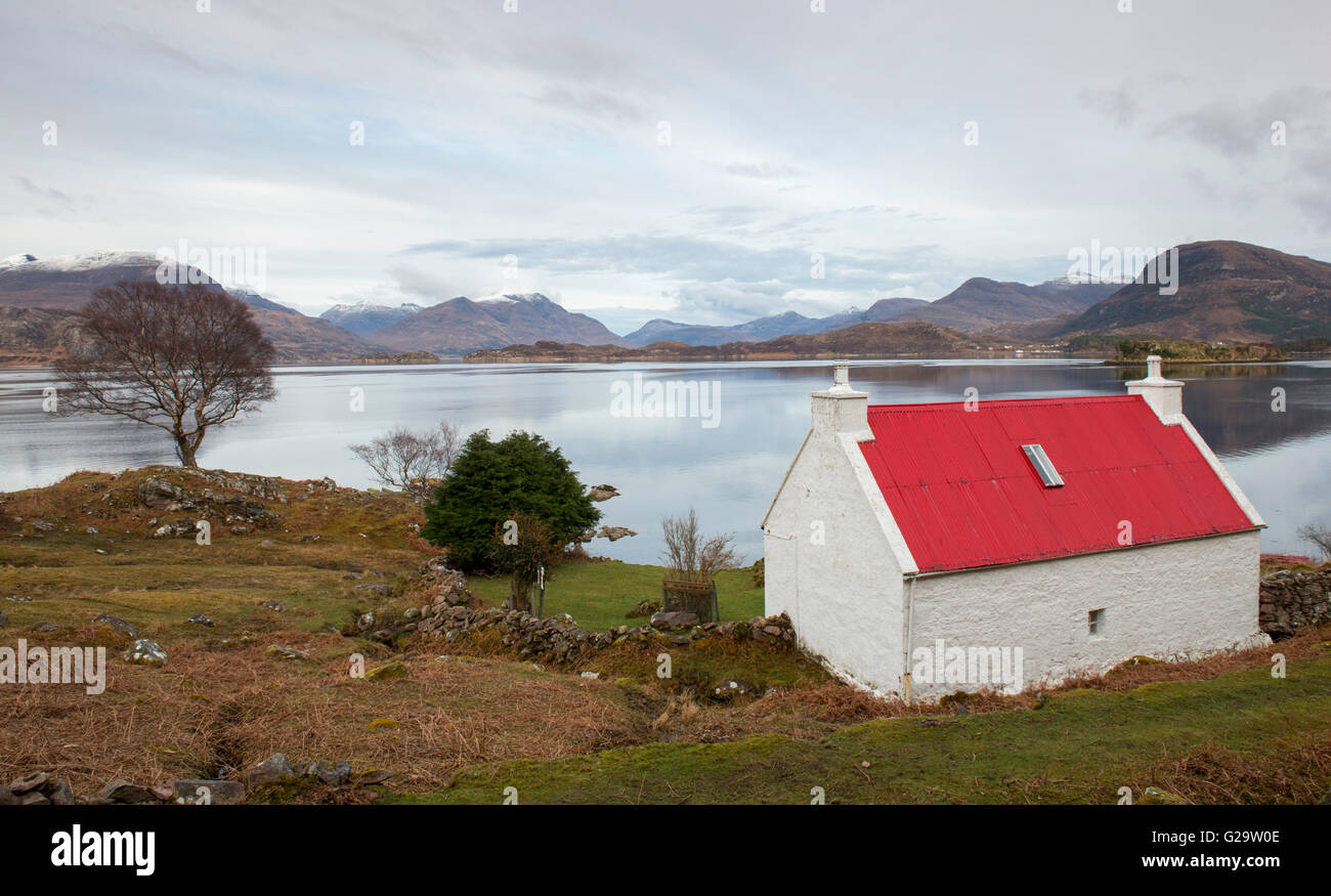 White cottage with a red roof, on the banks of Loch Shieldaig in Wester ...