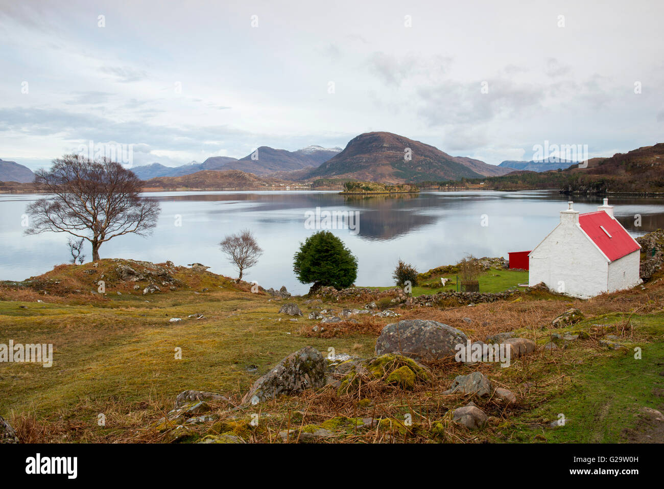 White cottage with a red roof, on the banks of Loch Shieldaig in Wester ...