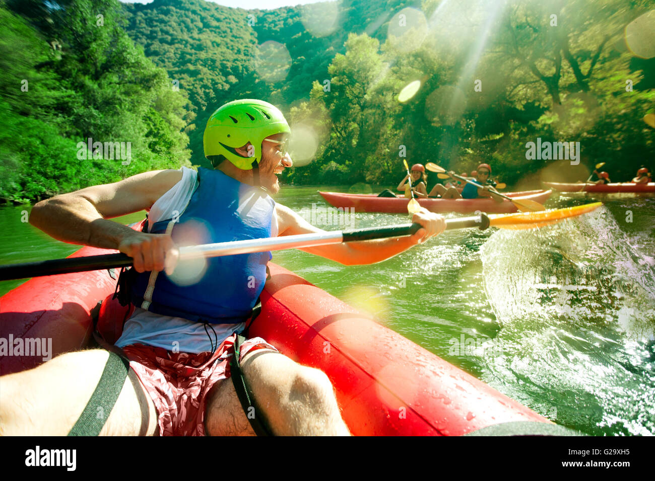 A young main in red inflatable canoe having fun splashing over his ...