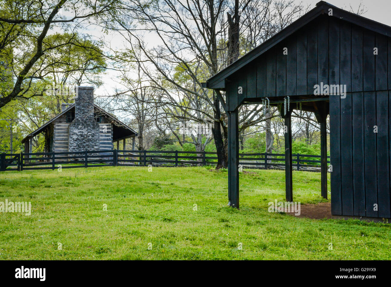 A Blacksmith's wooden horse stall in foreground with log cabin on farm ...