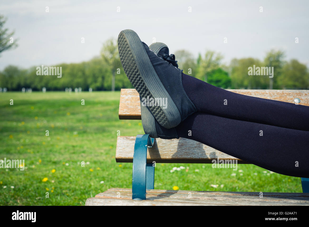 The legs of a young woman as she is lying on a bench in the park ...