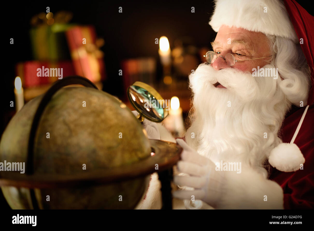 Santa Claus looking through magnifying glass at globe Stock Photo - Alamy