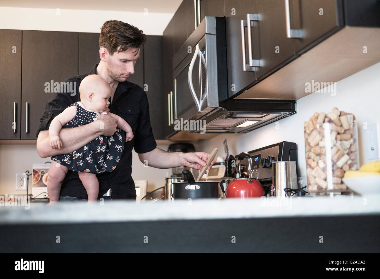 Father holding baby daughter (2-5 months) while stirring food Stock ...