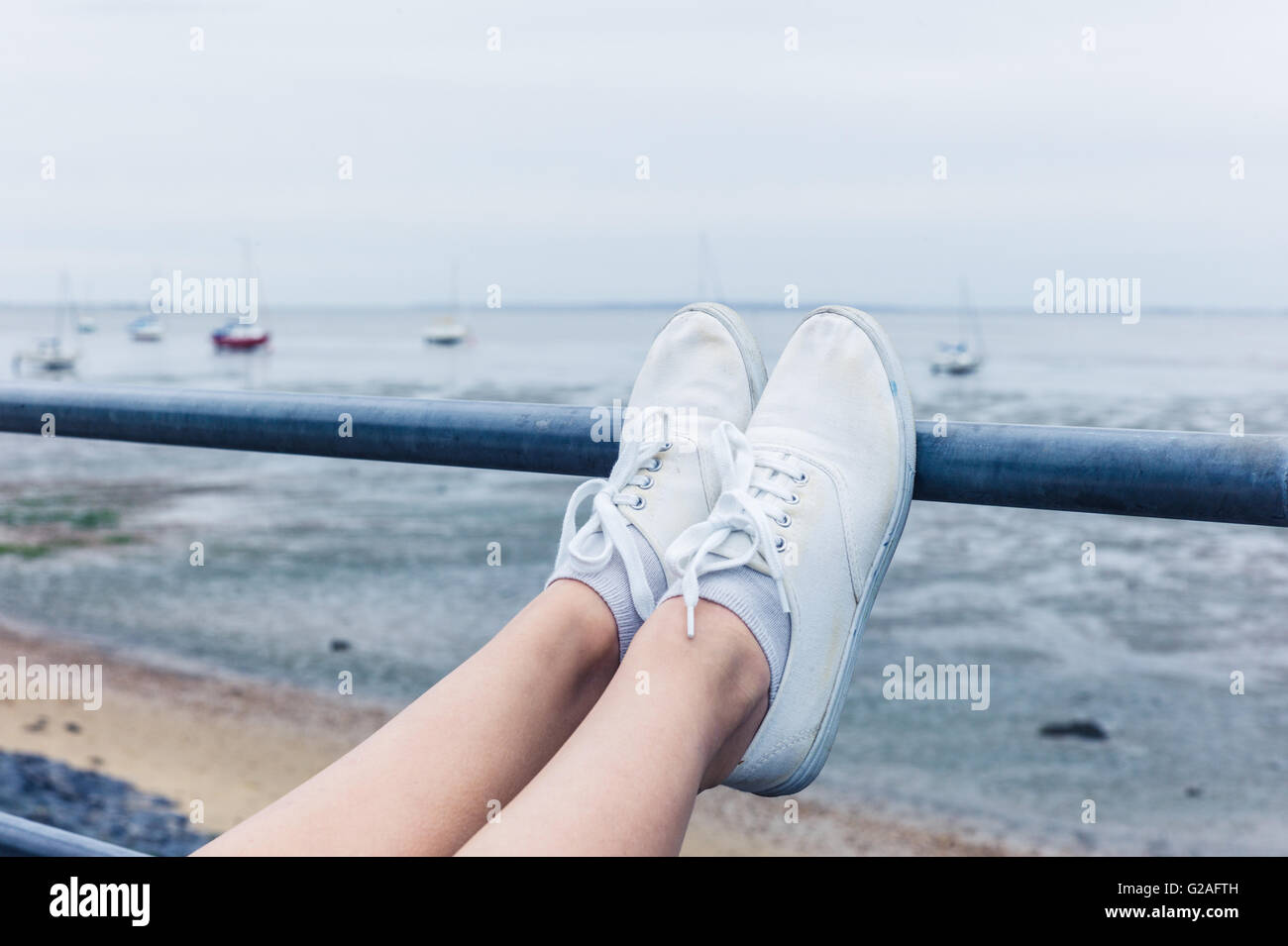 A young woman is resting her feet on a railing by the sea Stock Photo ...