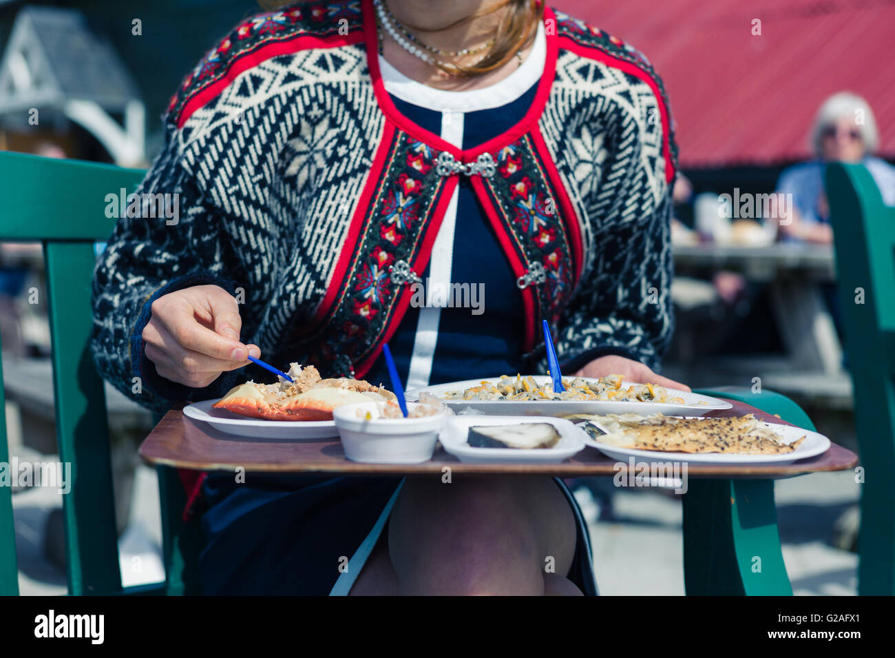 A young woman is eating cockles and smoked fish outside on a sunny day ...